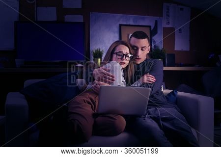 A Couple Is Sitting On A Couch And Looking At A Computer. The Couple ...