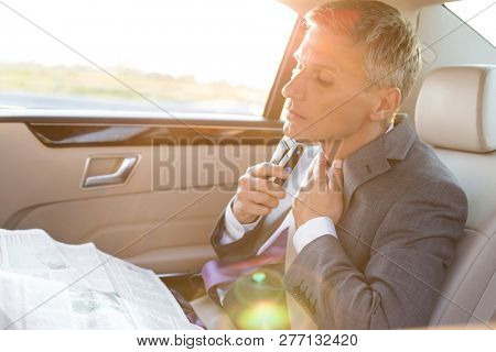 Businessman trimming while reading newspaper in car with a lens flare ...