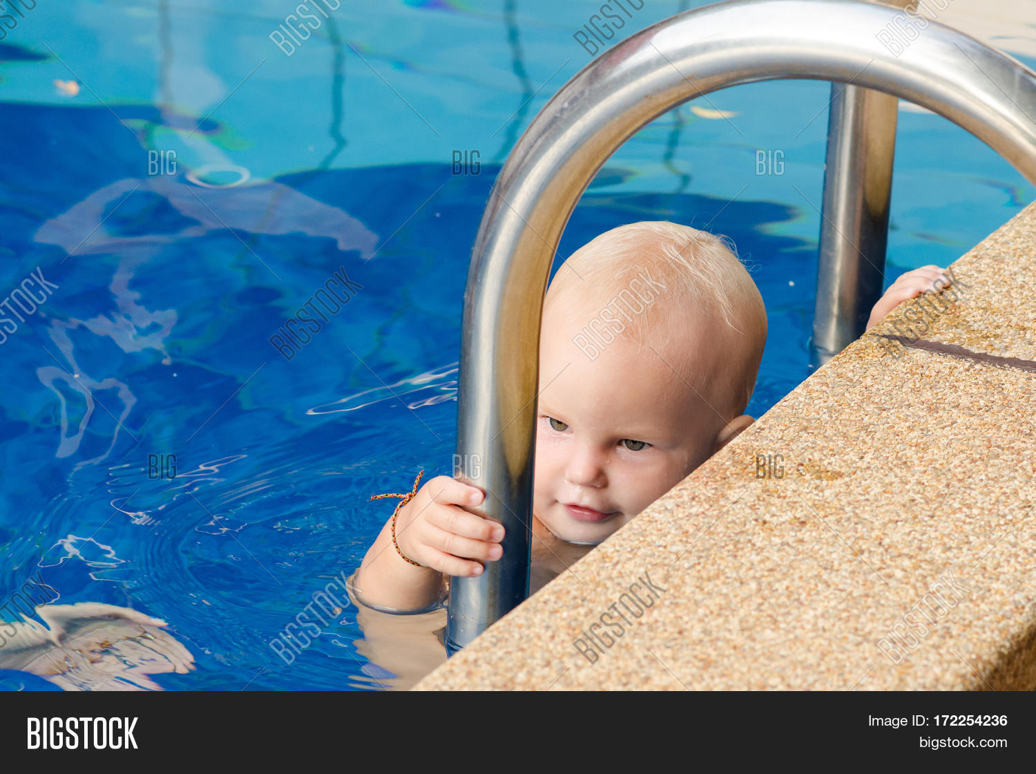 Small child tries to climb out of the pool. The girl holds hands for a ...